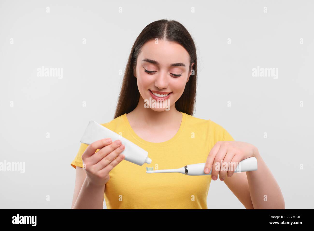 Happy young woman squeezing toothpaste from tube onto electric ...