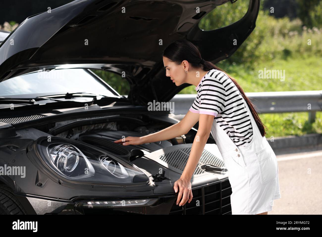 Stressed woman looking under hood of broken car outdoors Stock Photo - Alamy