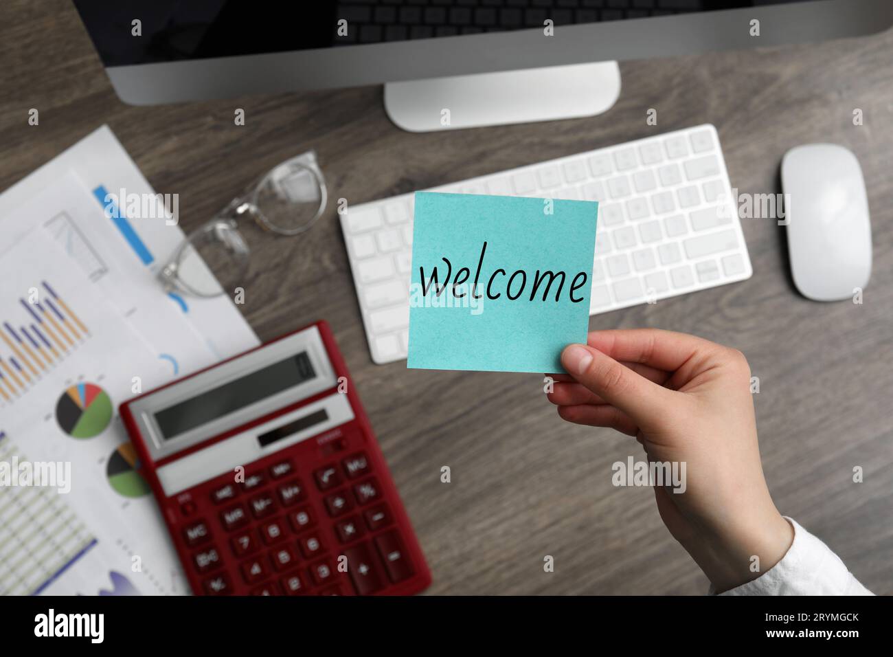 Woman holding paper note with word Welcome over her office desk, top ...