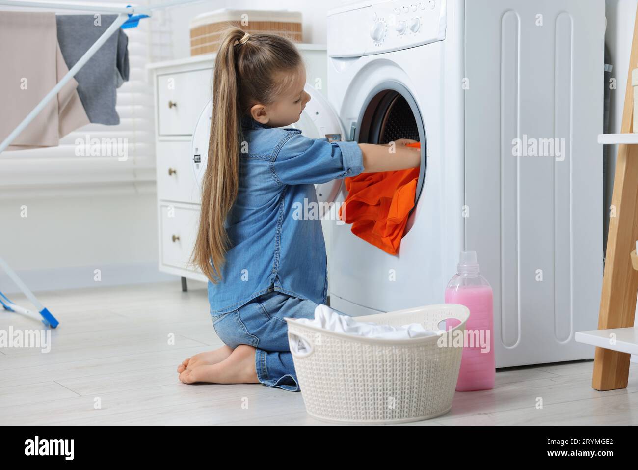 Little girl putting dirty clothes into washing machine in bathroom ...