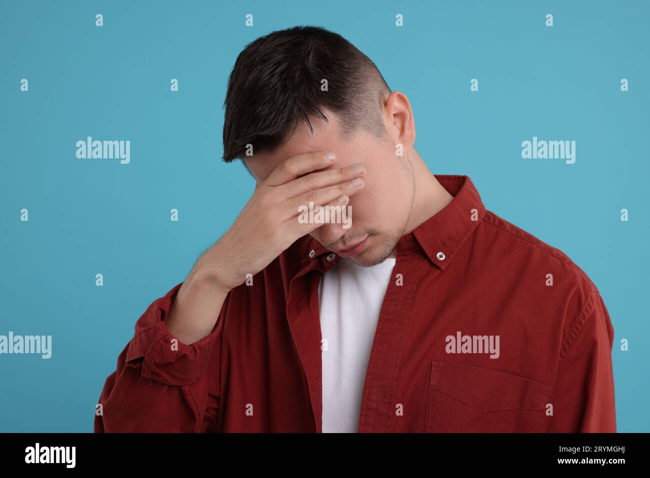 Embarrassed man covering face with hand on light blue background Stock ...