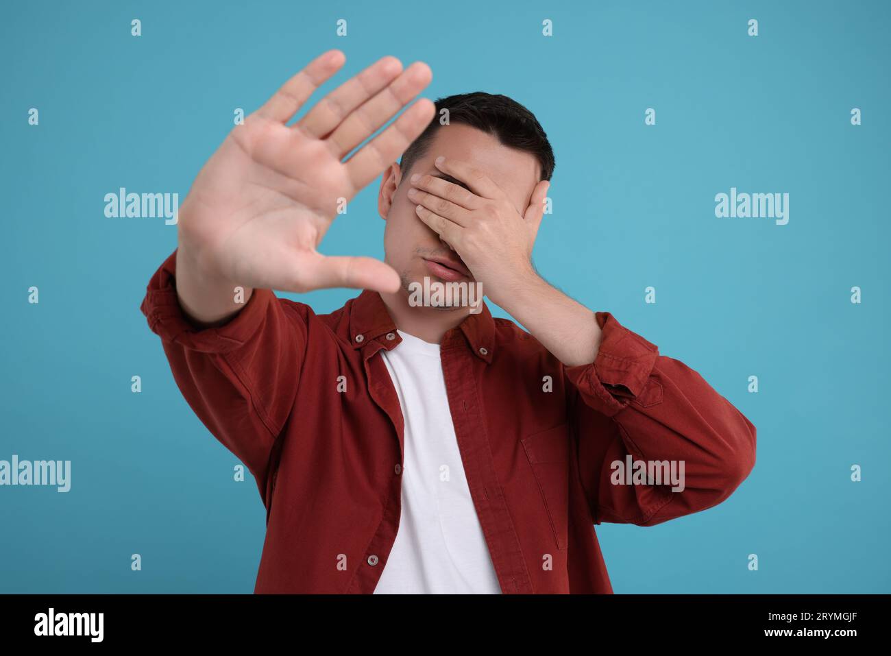 Embarrassed man covering face with hand on light blue background Stock ...