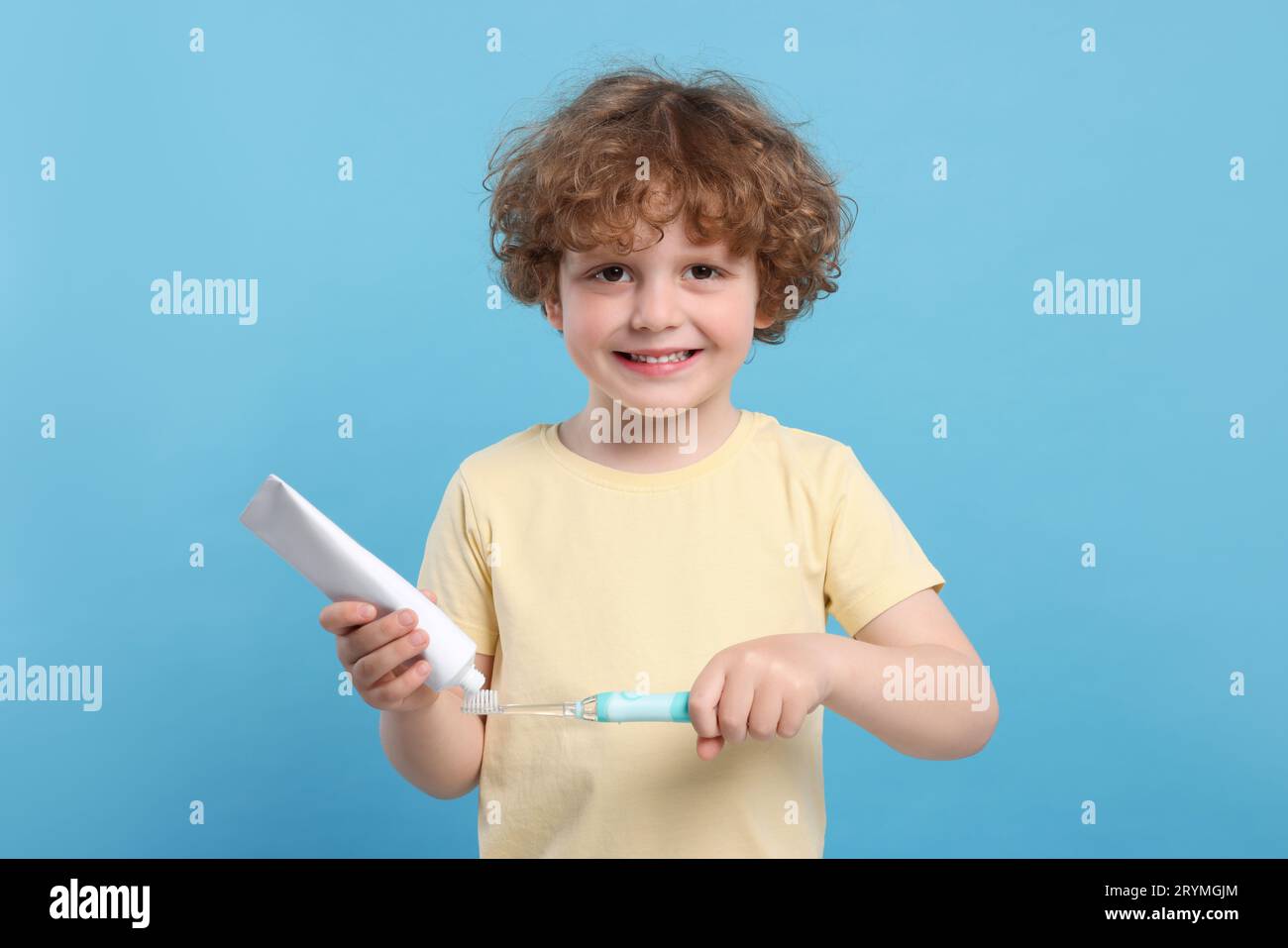 Cute little boy squeezing toothpaste from tube onto electric toothbrush ...