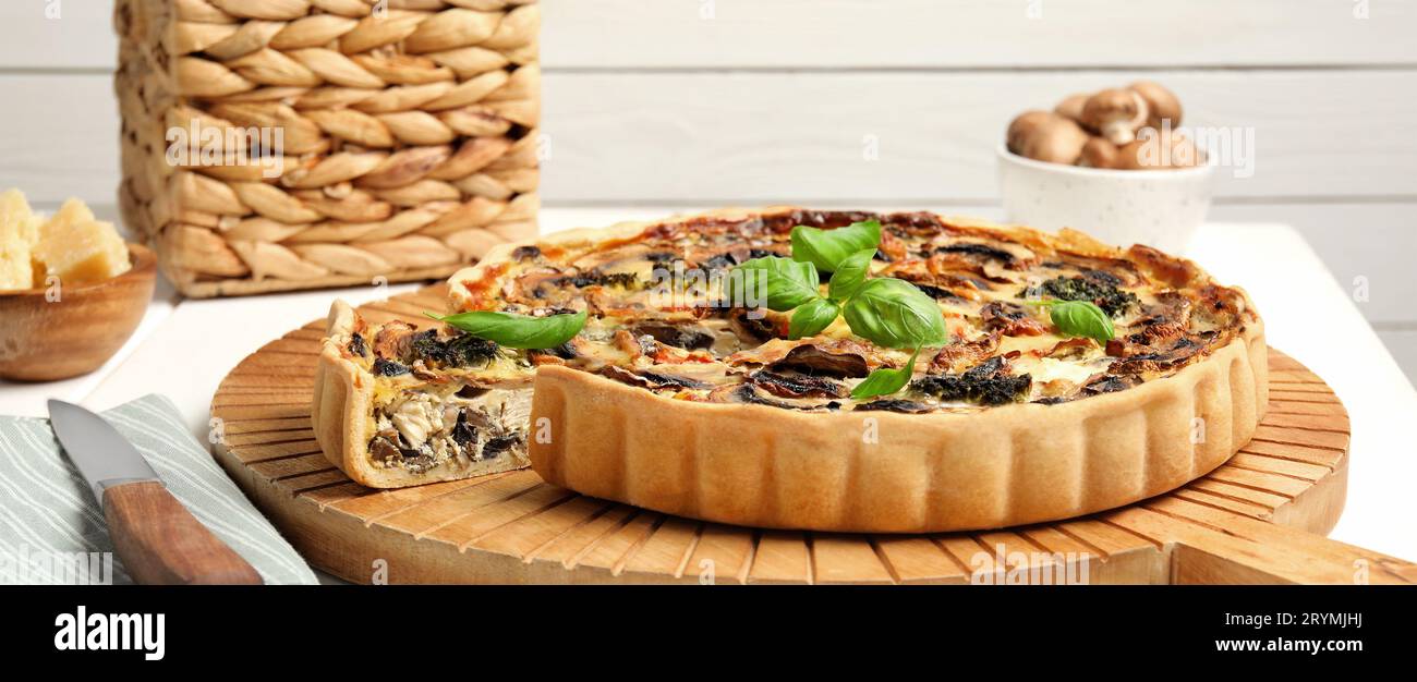 Delicious quiche with mushrooms and basil on white wooden table. Banner ...