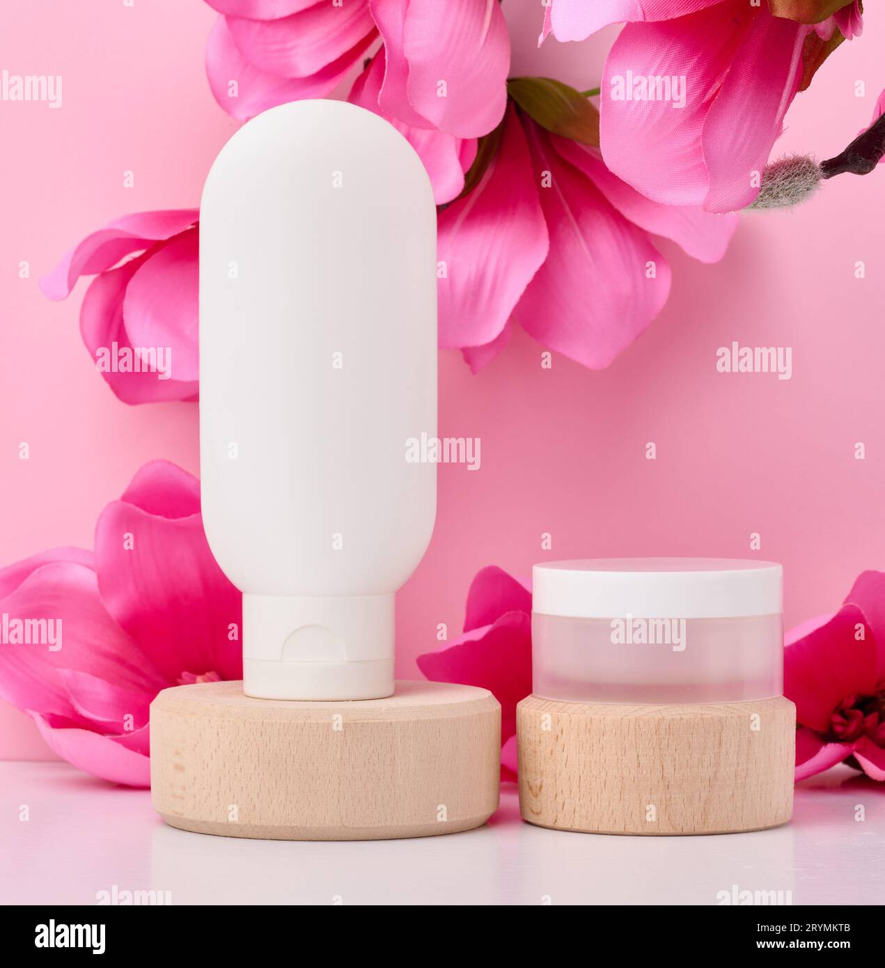 White plastic tube and jar for liquid cosmetics on a pink background ...