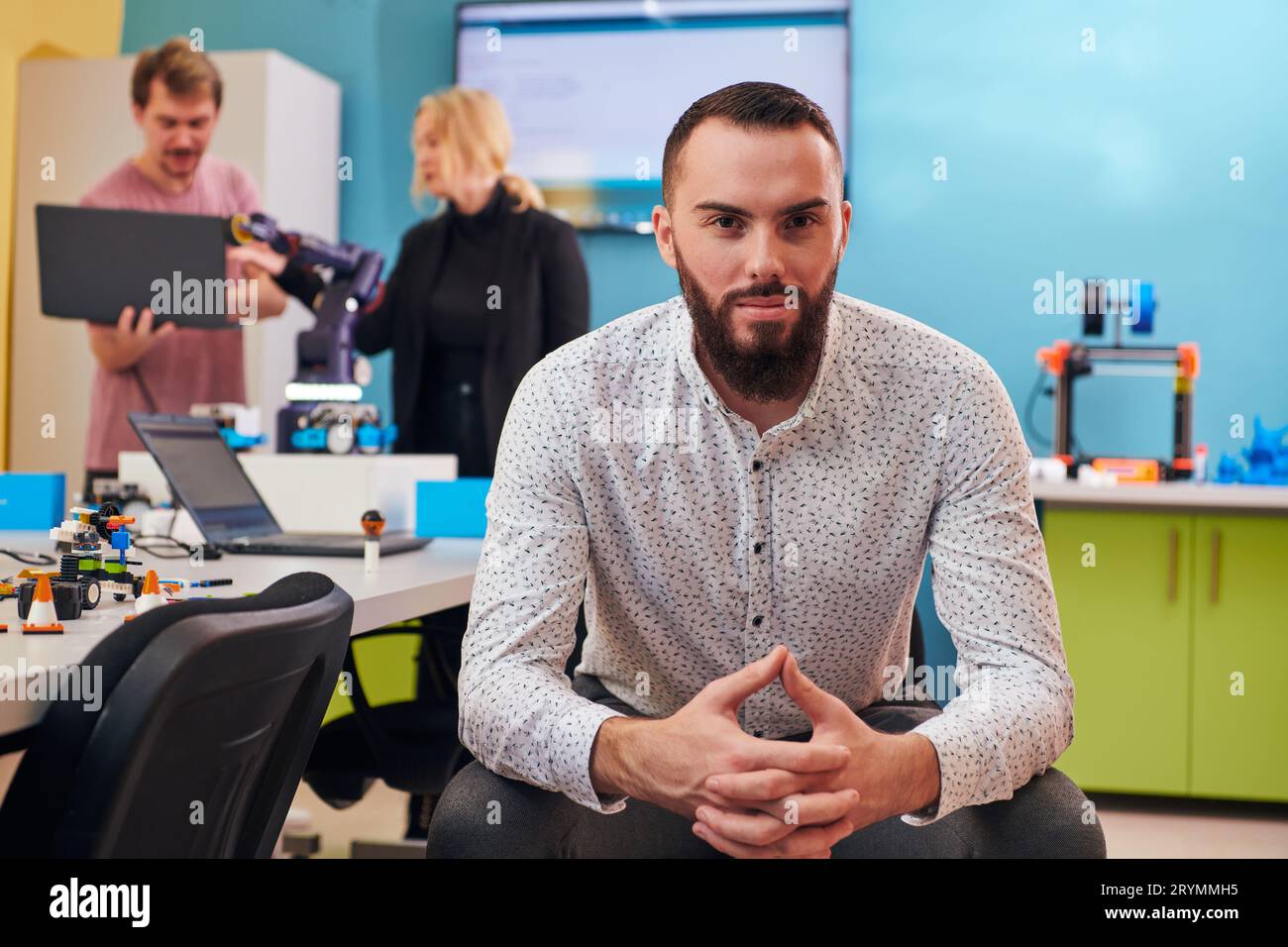 A man sitting in a robotics laboratory while his colleagues in the ...