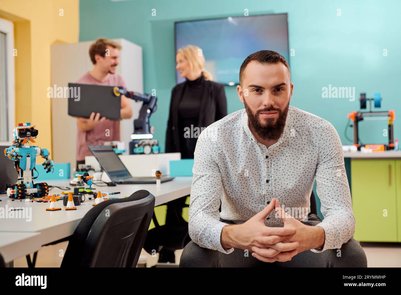 A man sitting in a robotics laboratory while his colleagues in the ...