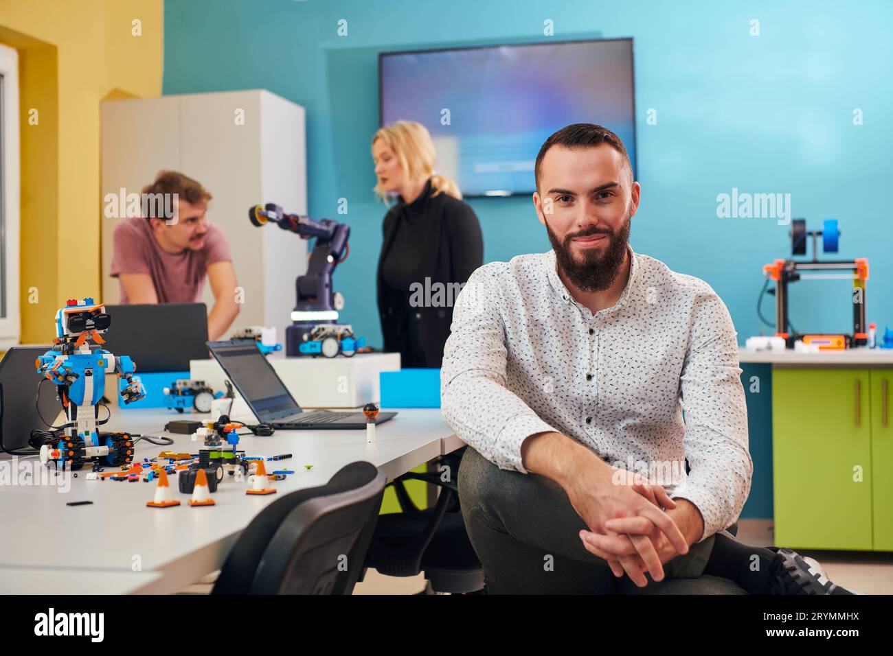 A man sitting in a robotics laboratory while his colleagues in the ...