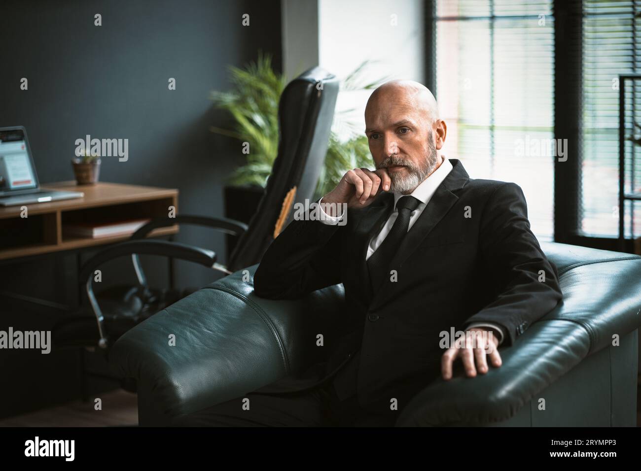 Sad mature man dressed in suit, sitting in chair, deep in thought ...