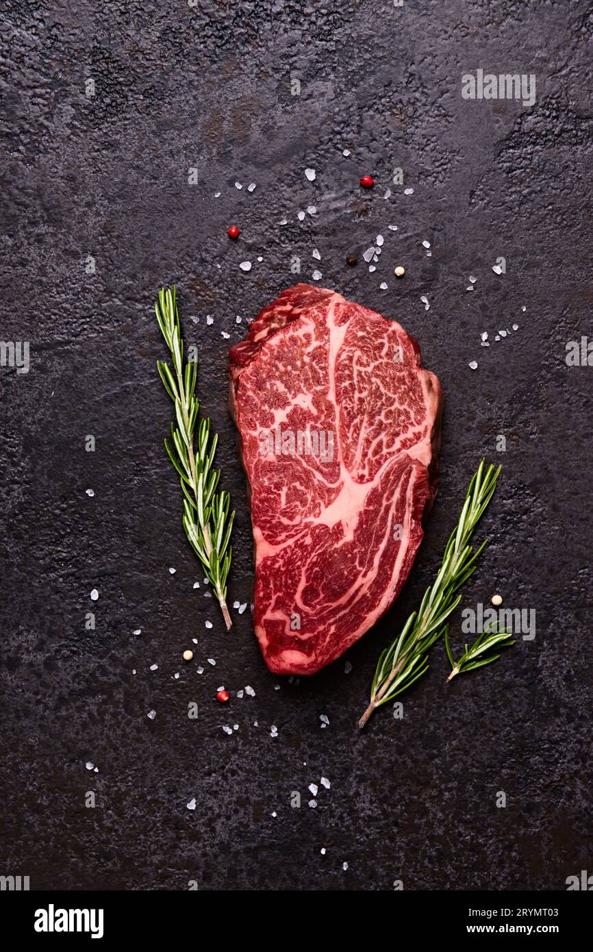 Fresh raw marbled beef rib eye steak and spices on black stone ...