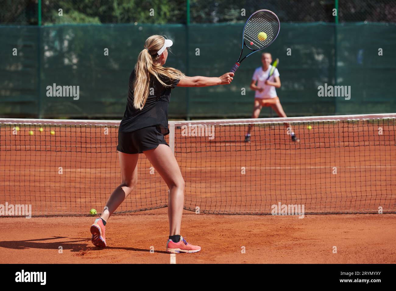 Young girls in a lively tennis match on a sunny day, demonstrating ...