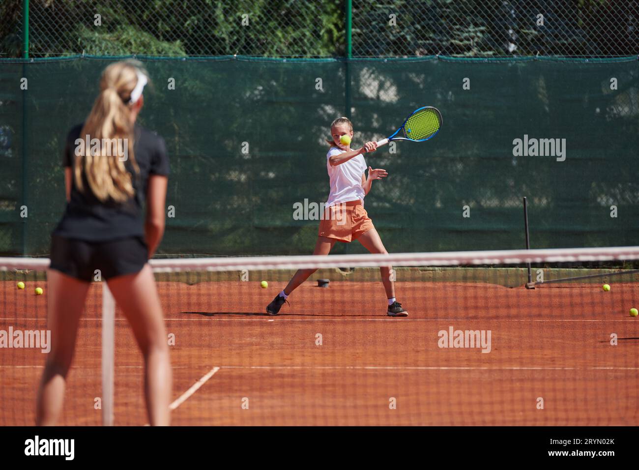Young girls in a lively tennis match on a sunny day, demonstrating ...