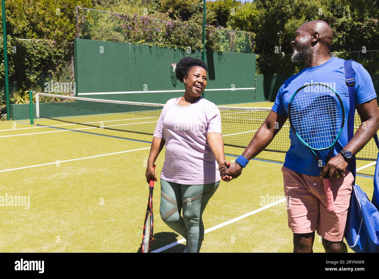 Happy senior african american couple with rackets walking holding hands ...