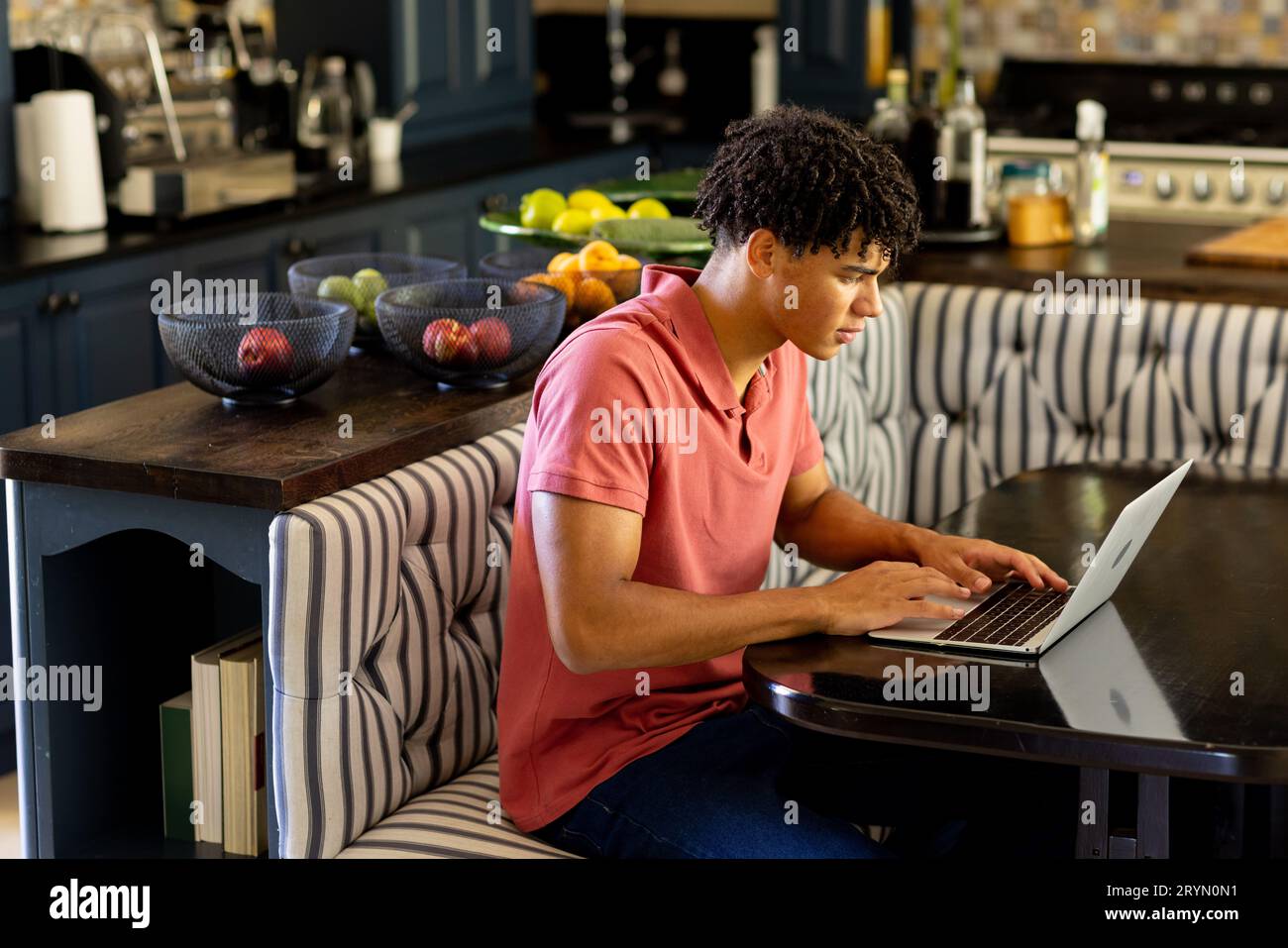 Side view of biracial young man with dreadlocks working over laptop on ...