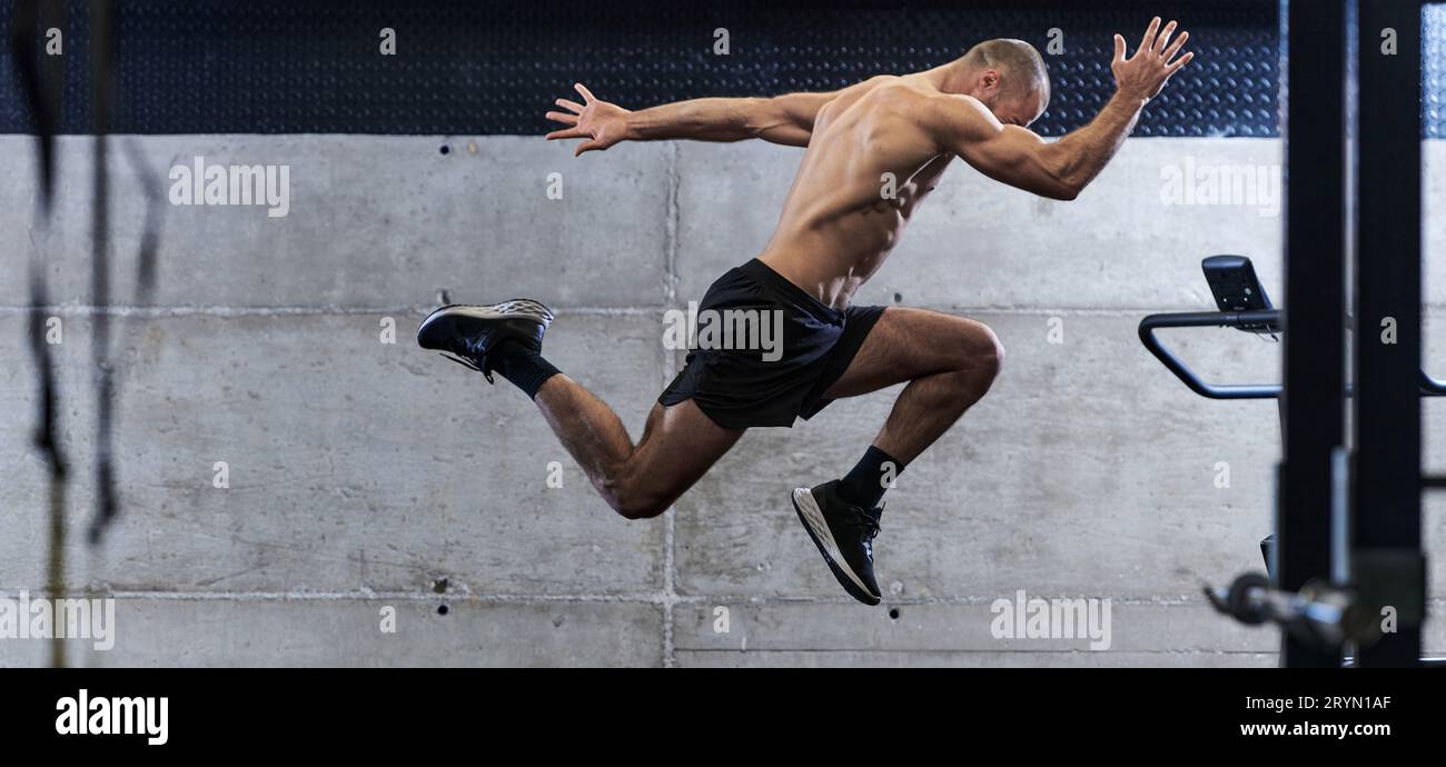 A muscular man captured in air as he jumps in a modern gym, showcasing ...