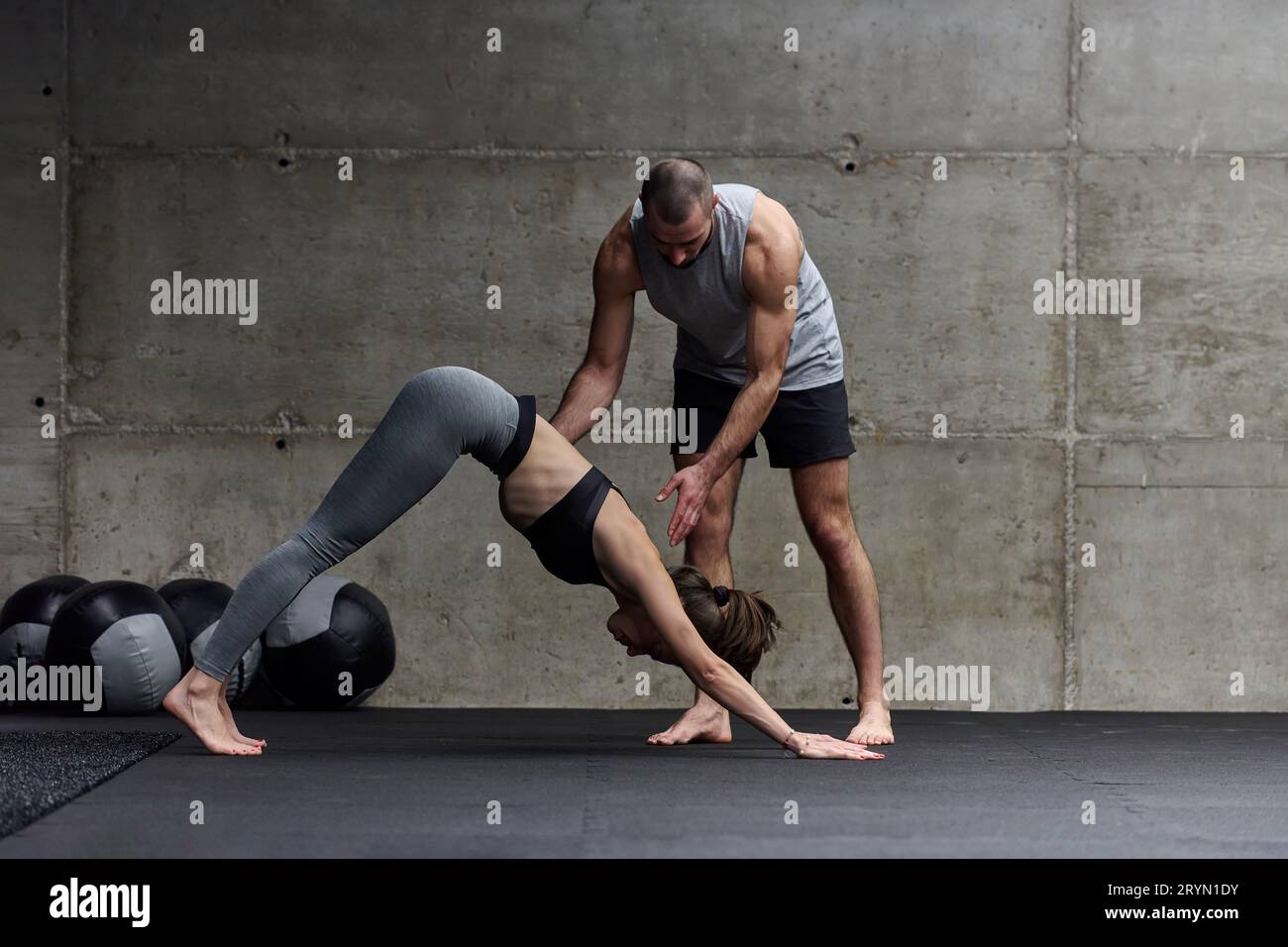 A muscular man assisting a fit woman in a modern gym as they engage in ...