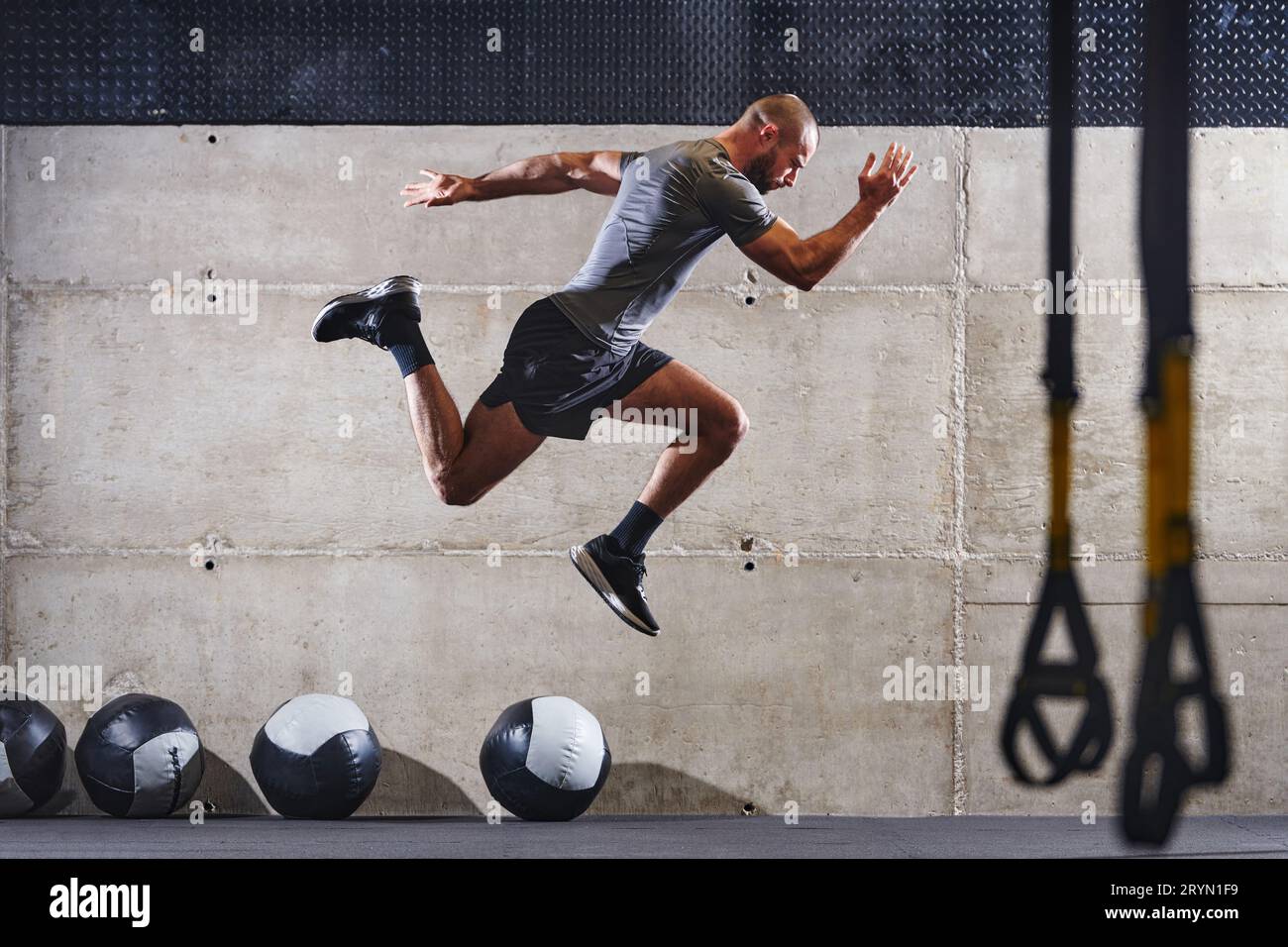 A muscular man captured in air as he jumps in a modern gym, showcasing ...