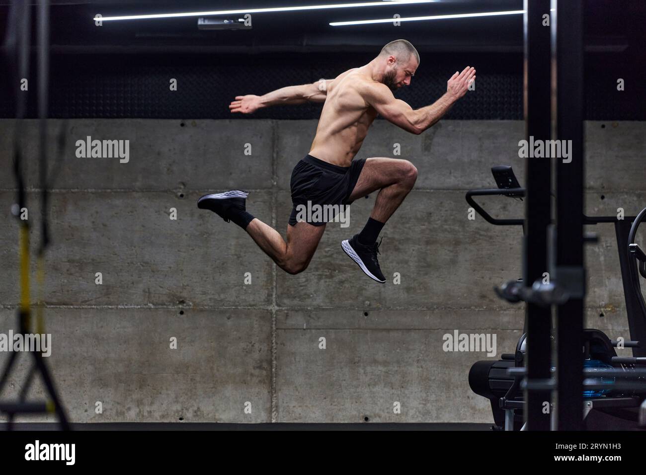 A muscular man captured in air as he jumps in a modern gym, showcasing ...