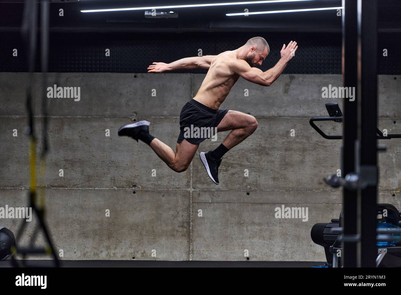 A muscular man captured in air as he jumps in a modern gym, showcasing ...