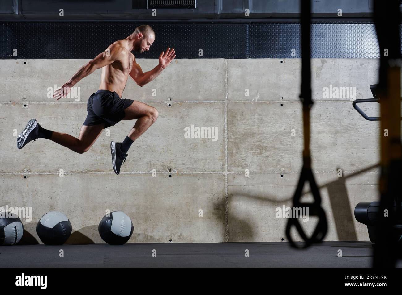 A muscular man captured in air as he jumps in a modern gym, showcasing ...