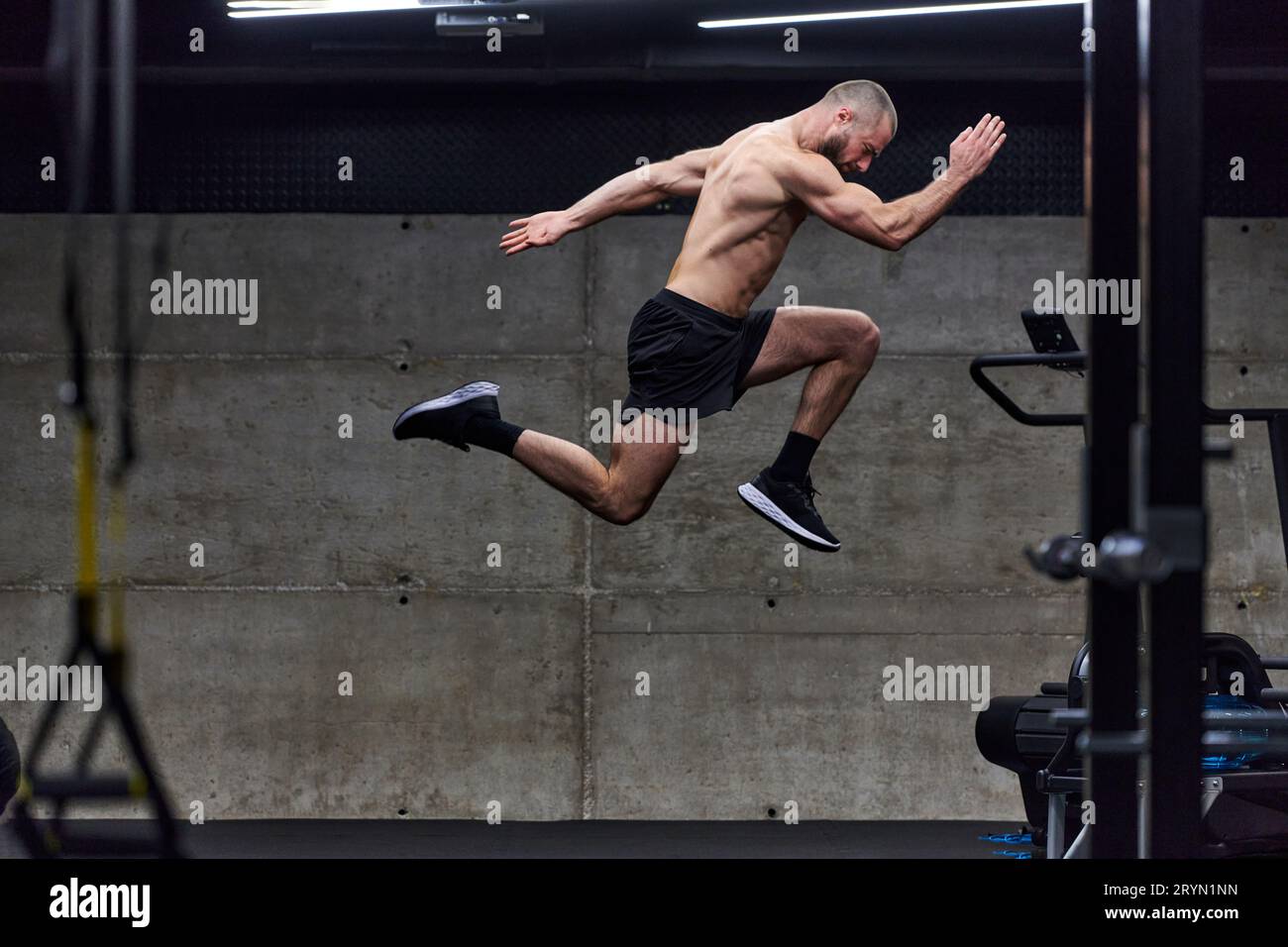 A muscular man captured in air as he jumps in a modern gym, showcasing ...