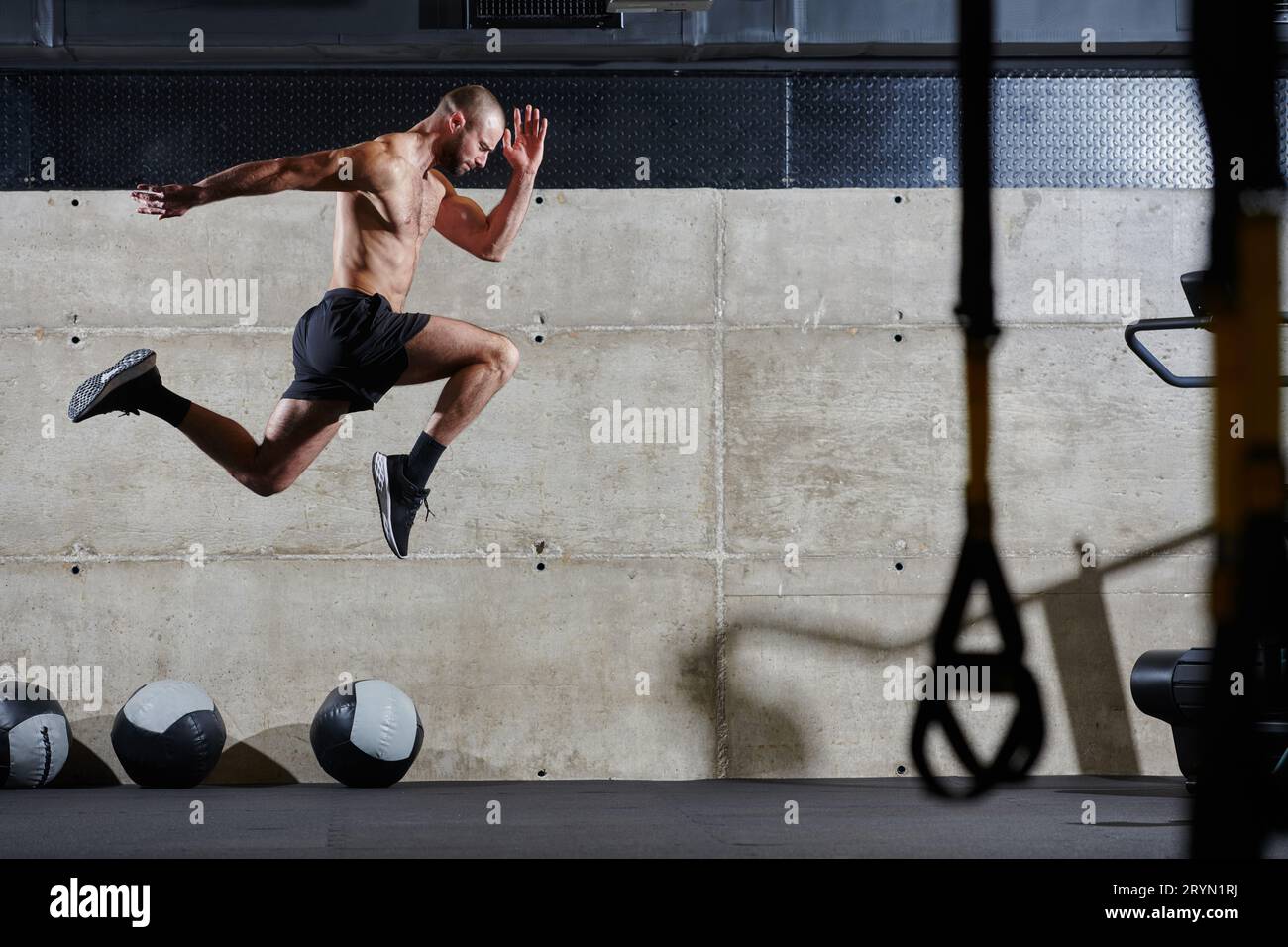 A muscular man captured in air as he jumps in a modern gym, showcasing ...