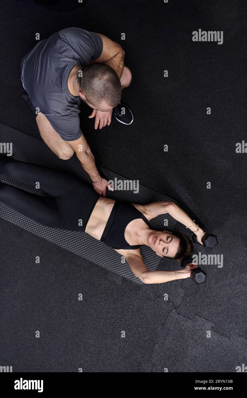 A muscular man assisting a fit woman in a modern gym as they engage in ...