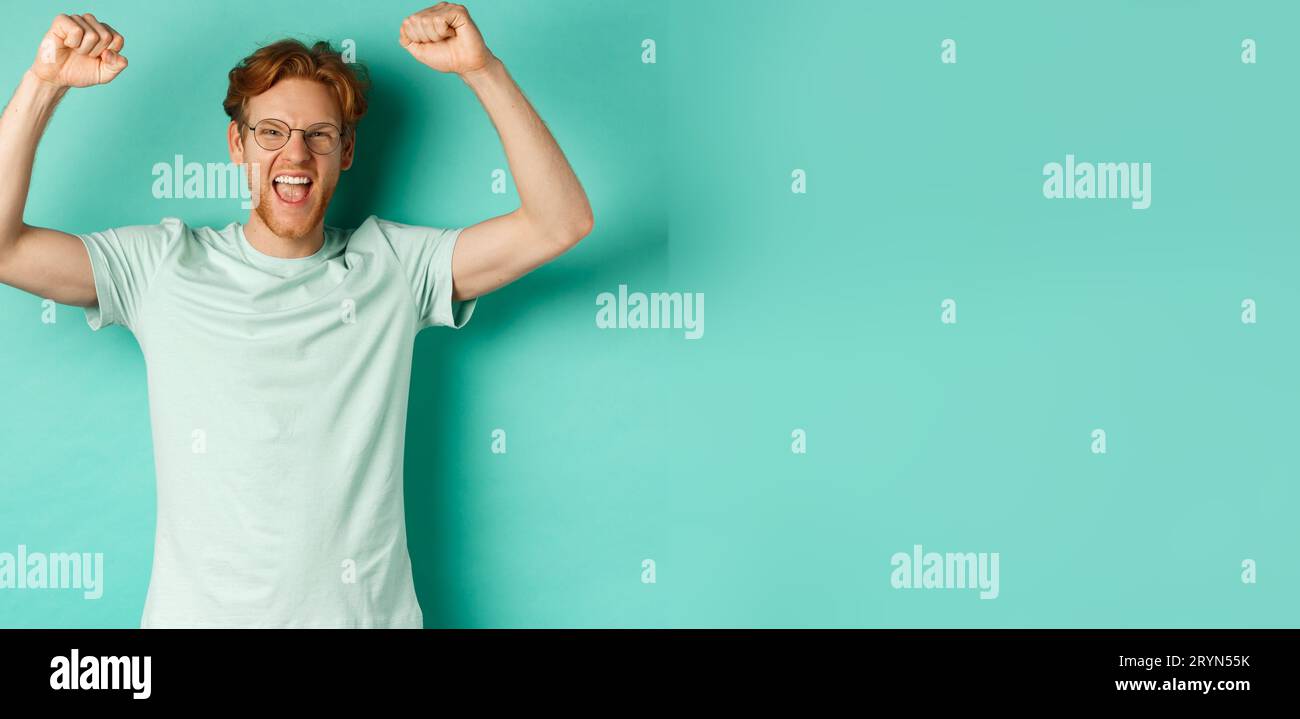 Image of young redhead man feeling like champion, raising hands up in ...