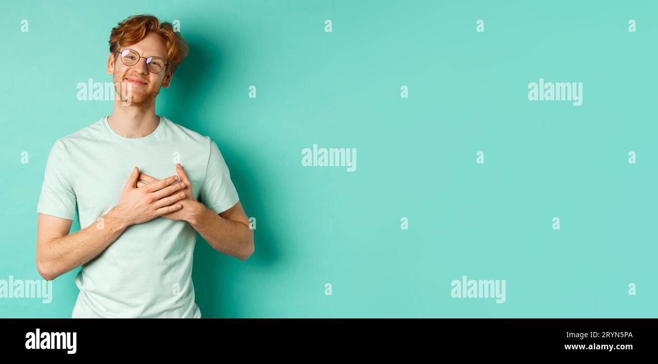 Handsome young man with red hair and glasses, holding hands on heart ...