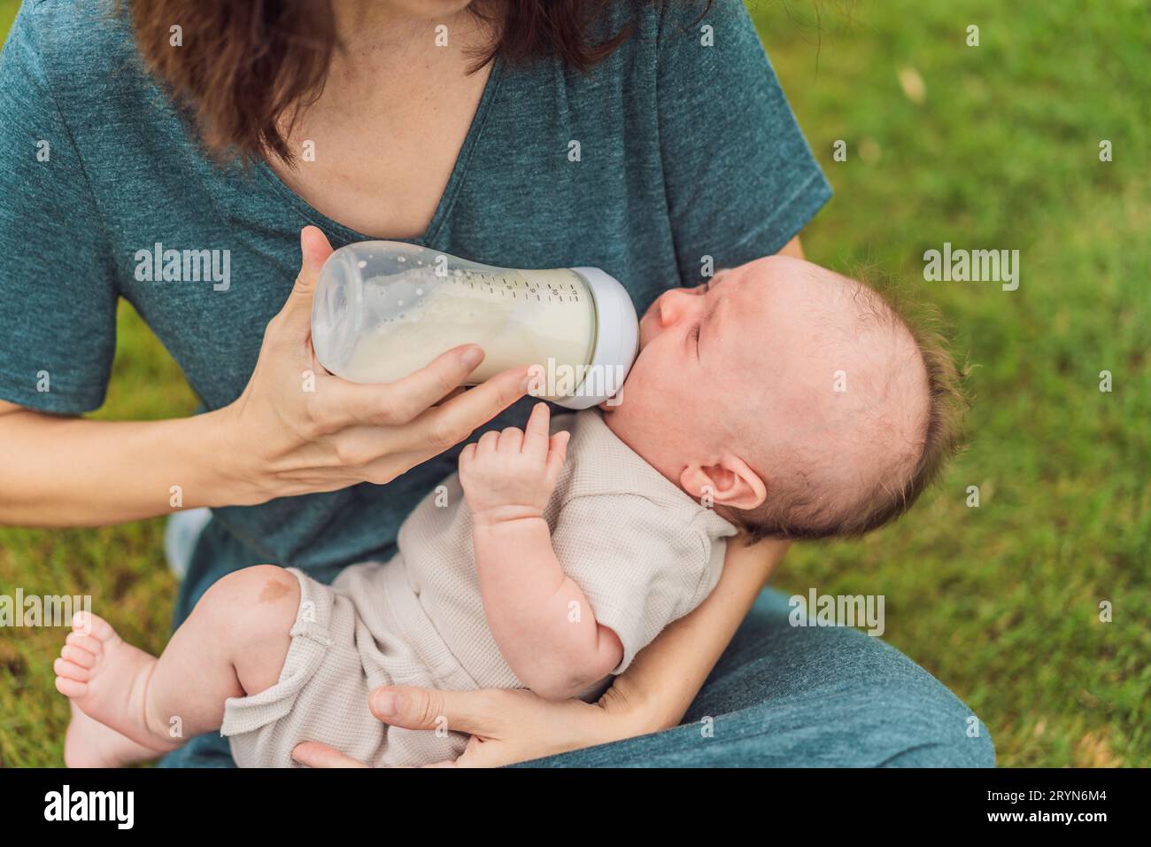 Mother holding and feeding baby from milk bottle in the park. Portrait ...