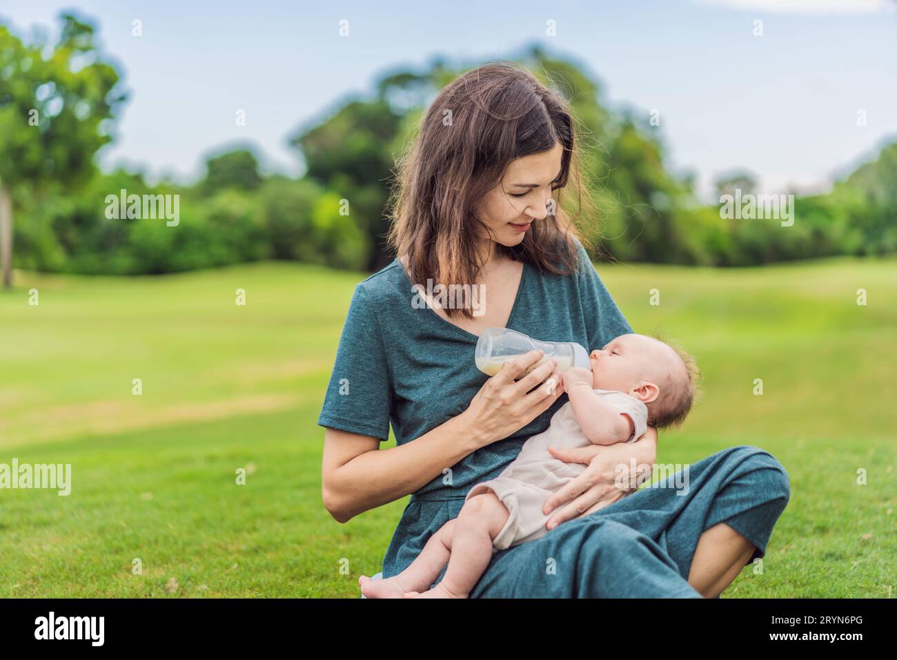 Mother holding and feeding baby from milk bottle in the park. Portrait ...