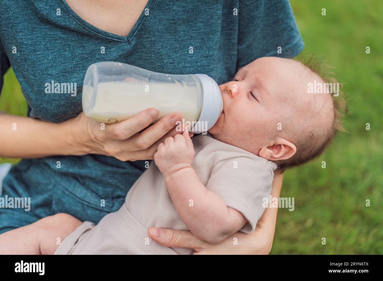 Mother holding and feeding baby from milk bottle in the park. Portrait ...