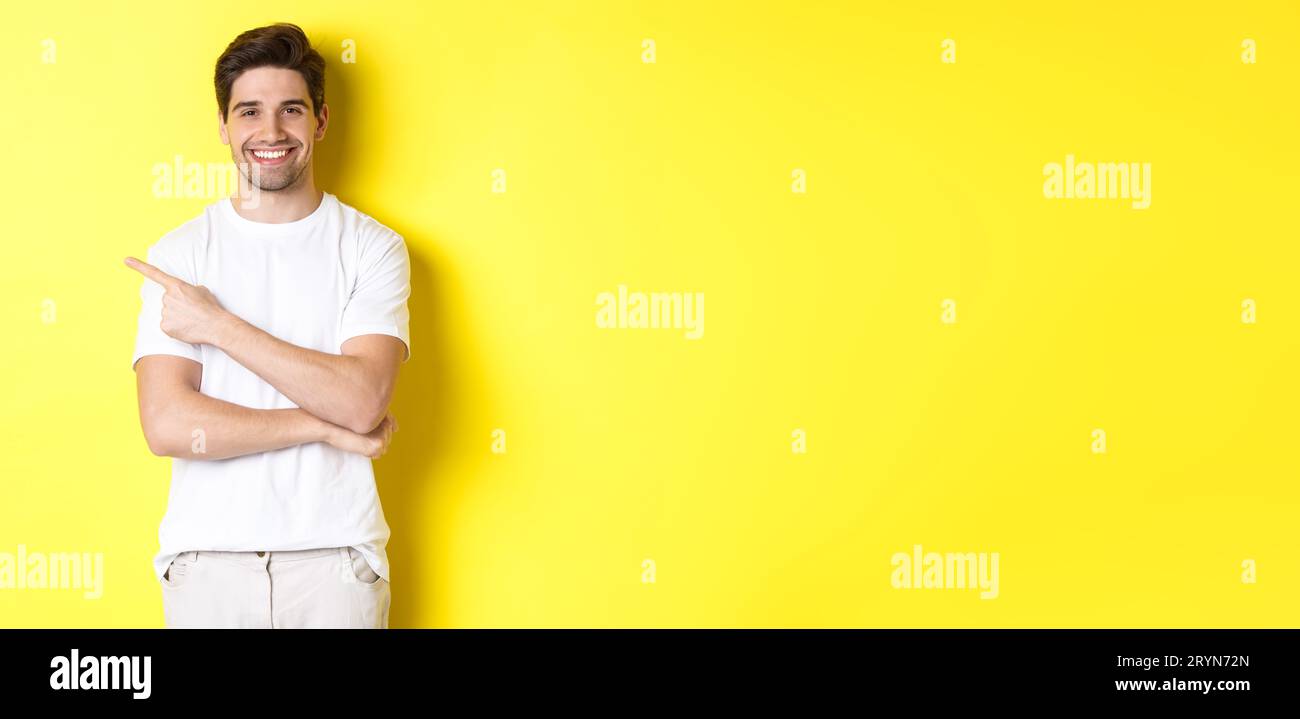 Handsome guy pointing left and smiling, showing advertisement on yellow ...