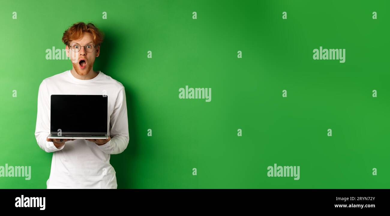 Surprised redhead man in glasses showing laptop blank screen, showing ...