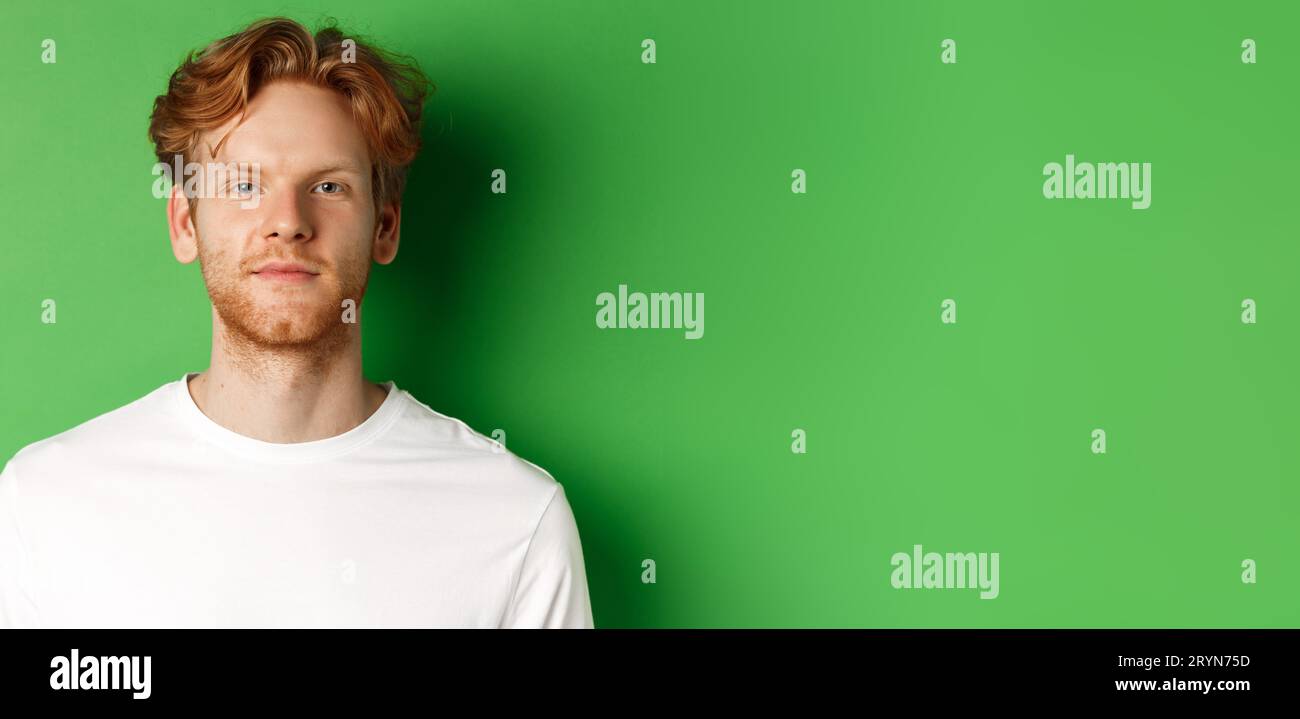 Close-up of young man with red messy hair and beard looking at camera ...