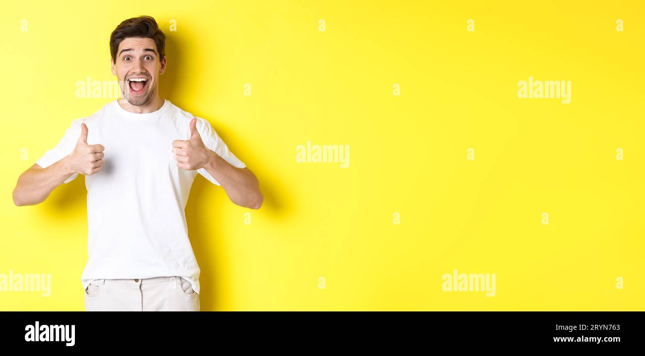 Excited handsome man showing thumbs up, approve and saying yes ...