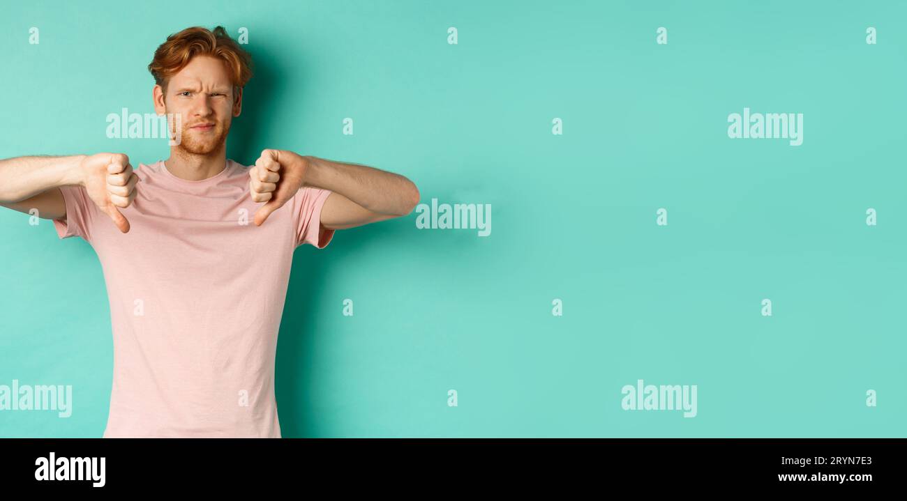 Disappointed guy with red hair showing thumbs-down, frowning and ...