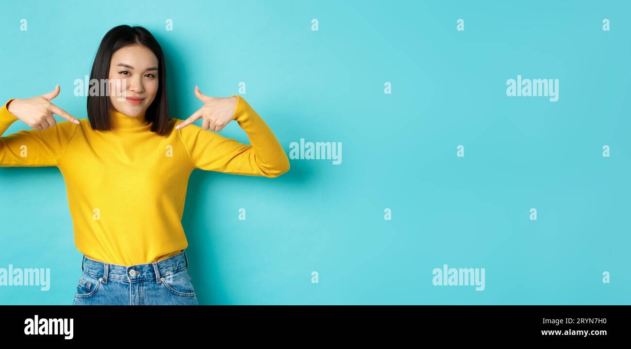 Confident asian woman in stylish sweater pointing fingers at logo on ...