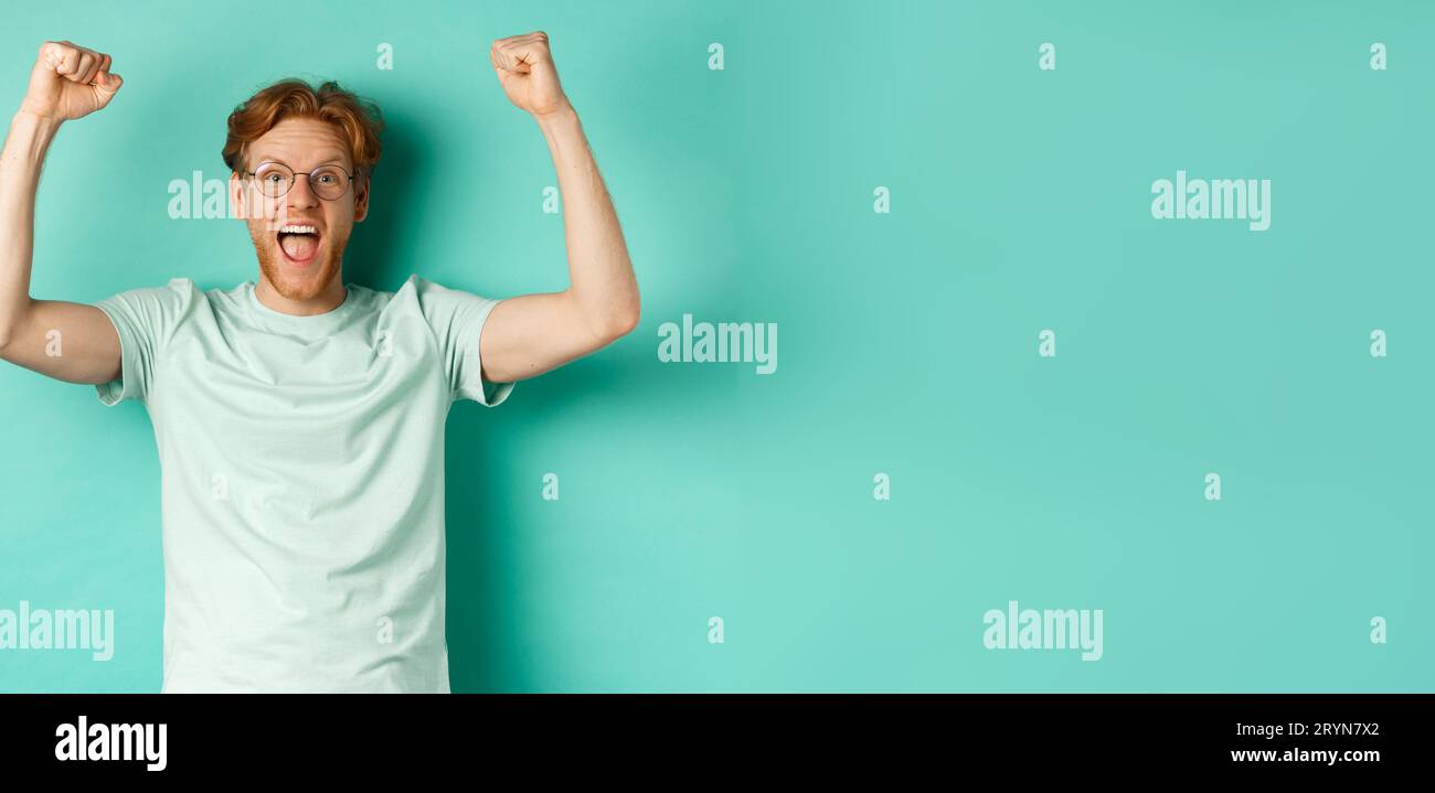 Young redhead man feeling like champion, raising hands up in fist pump ...