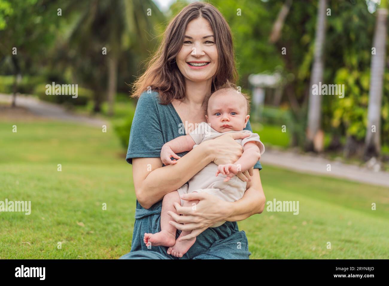 A happy 40-year-old mother cradles her newborn in a sun-drenched park ...
