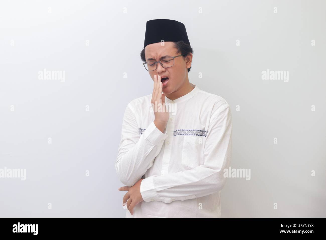 Portrait of young Asian muslim man yawning with hand covering his mouth ...
