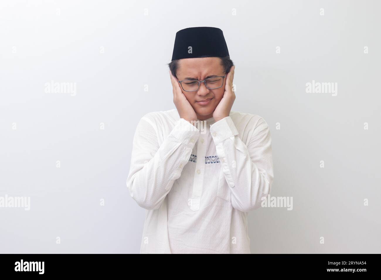 Portrait of young Asian muslim man covering ears with fingers with ...