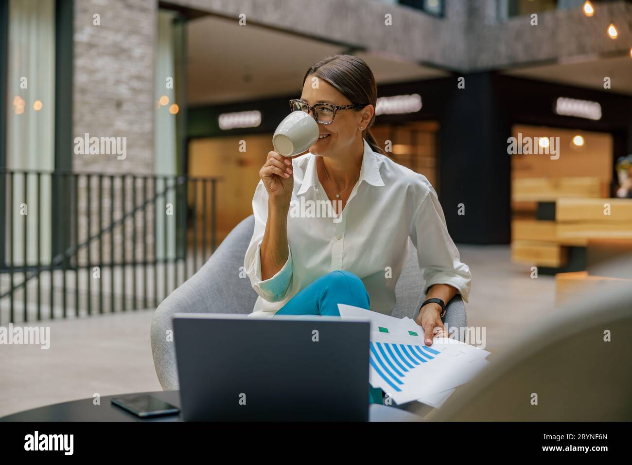 Smiling female analyst drinks coffee working with documents and use ...