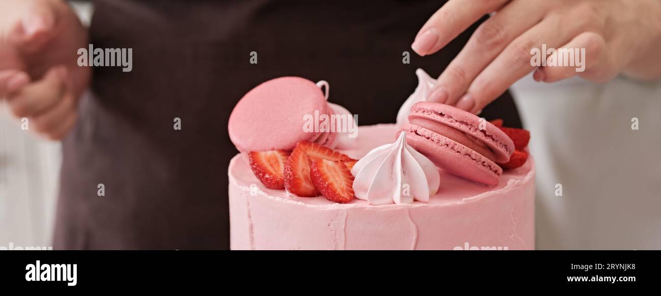 Woman pastry chef decorates pink cake with macaroons and berries, close ...