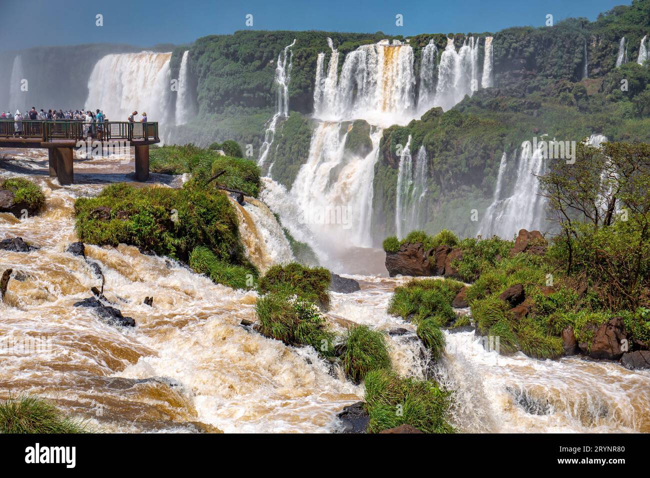 View to spectacular Iguazu Falls with visitor platform and blue sky ...