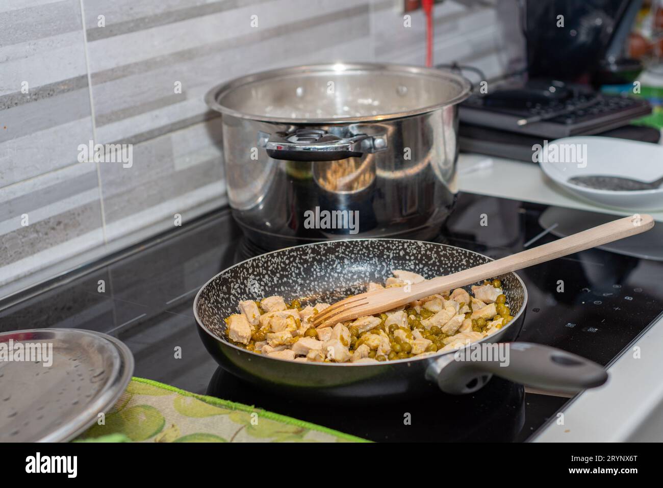 Chicken and peas are cooking in a pan on an induction cooker. Typical ...