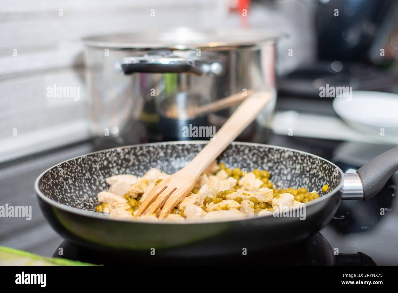 Chicken and peas are cooking in a pan on an induction cooker. Typical ...