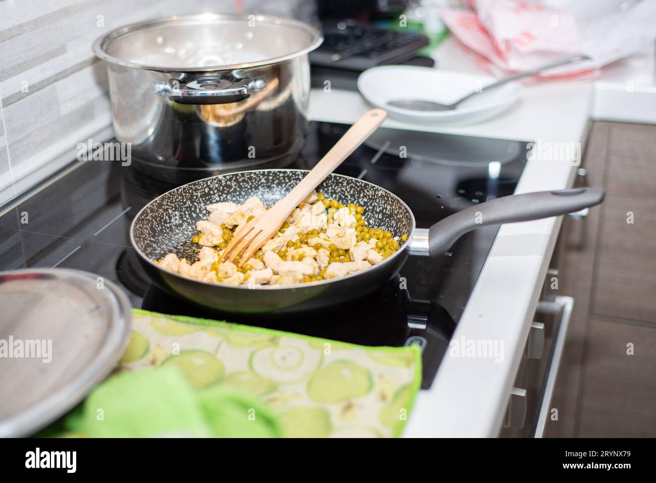 Chicken and peas are cooking in a pan on an induction cooker. Typical ...