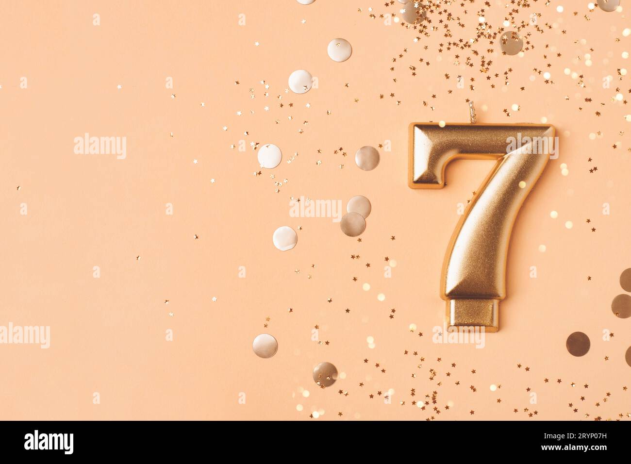 Gold candle in the form of number seven on peach background with ...