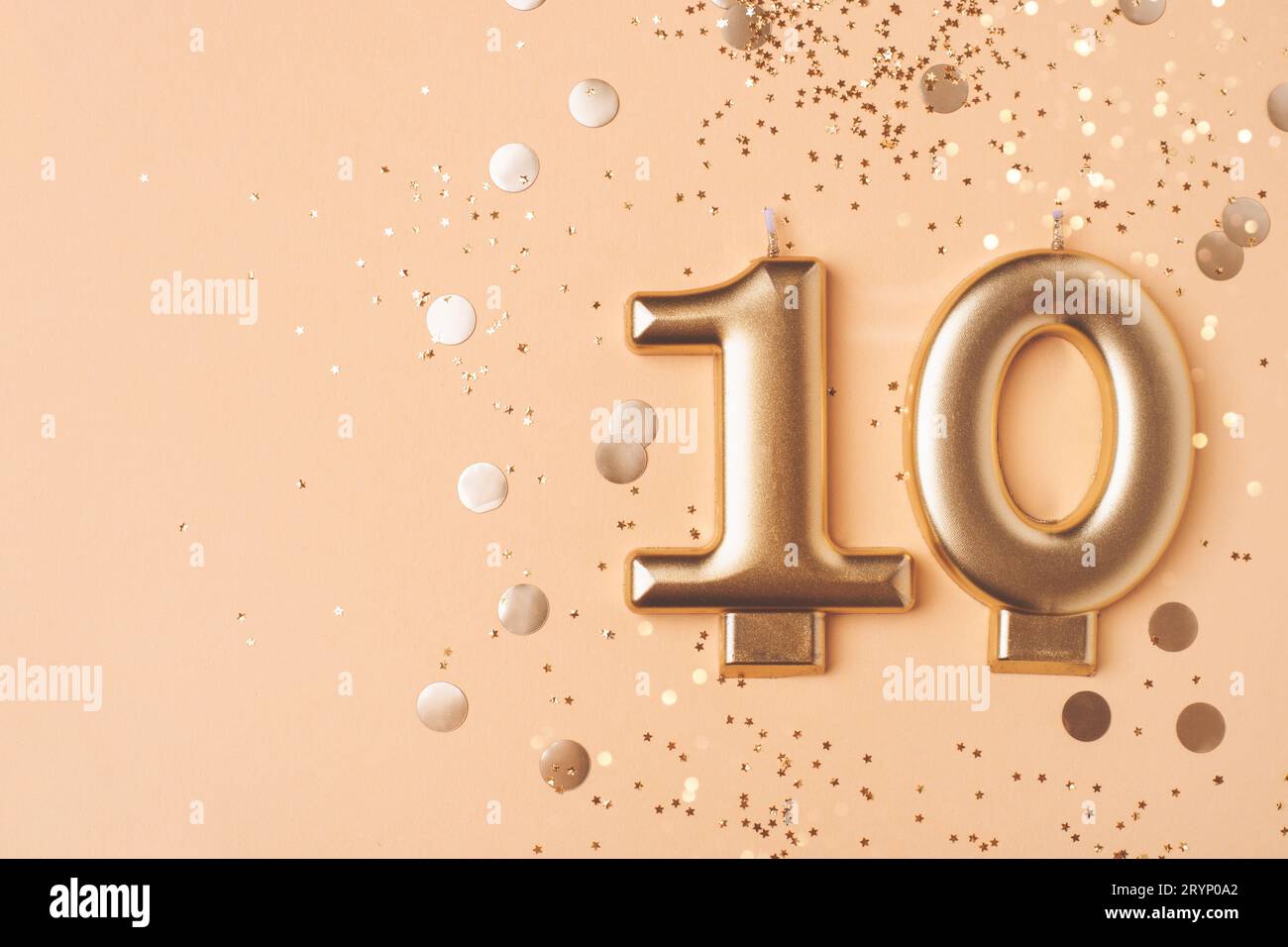 Gold candle in the form of number ten on peach background with confetti ...